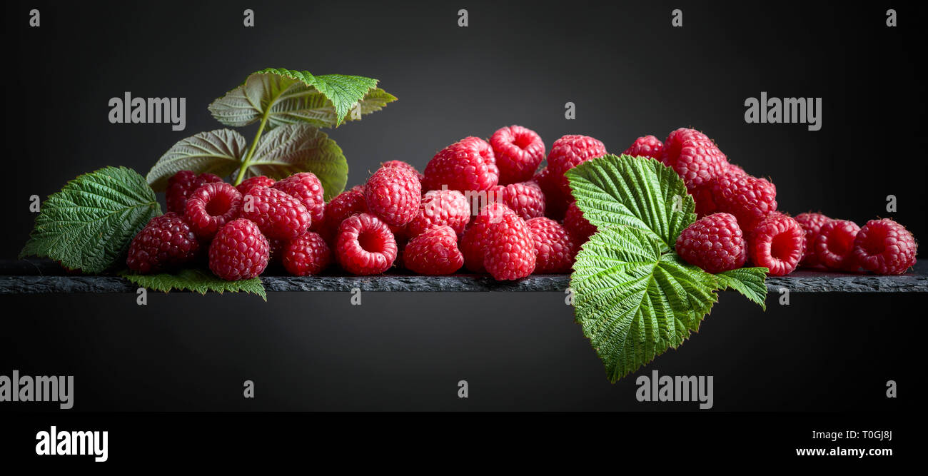 Raspberry with green leaves on a dark background Stock Photo - Alamy