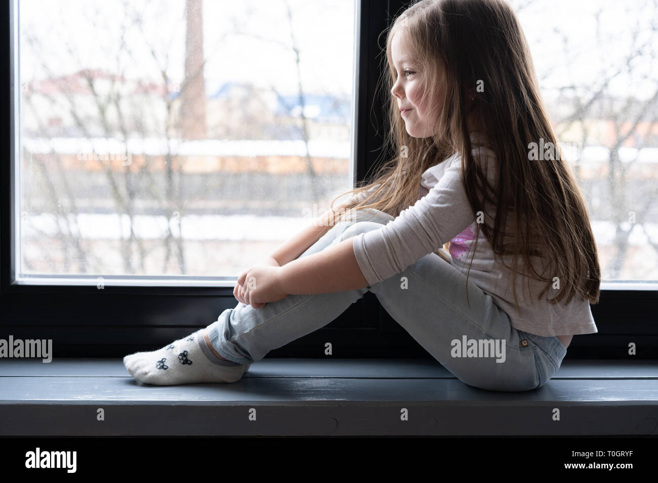 Adorable little girl sitting by the window Stock Photo - Alamy