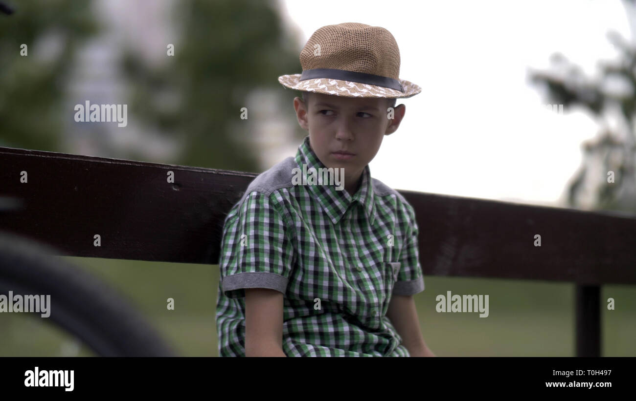 angry, unhappy suspicious boy sitting on a bench in the park, a boy ...