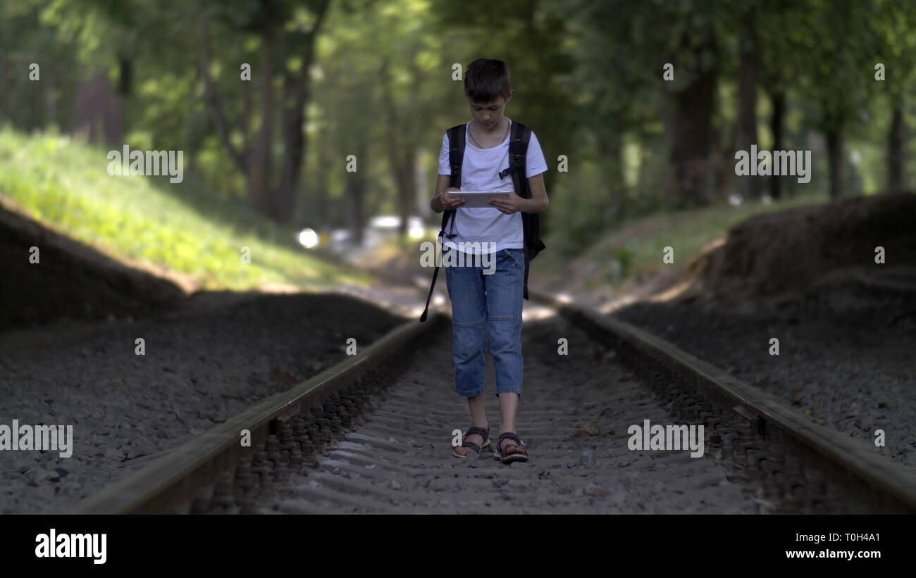 traveler boy is walking along the railroad tracks looks at the tablet ...