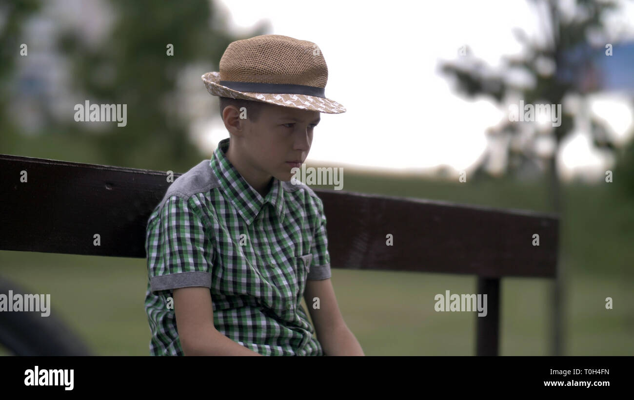 angry, unhappy suspicious boy sitting on a bench in the park, a boy ...