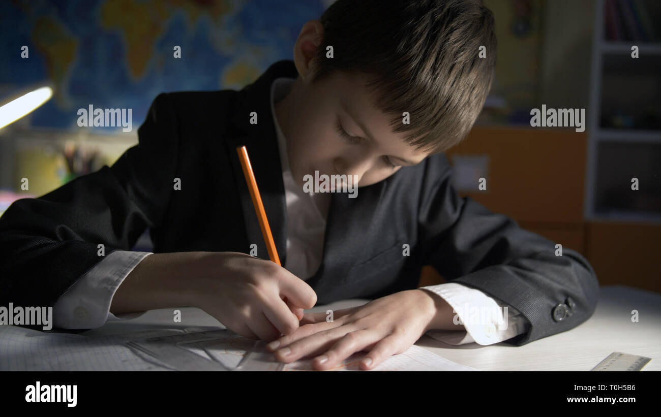 boy doing homework at home in the evening, sits at the table in a ...