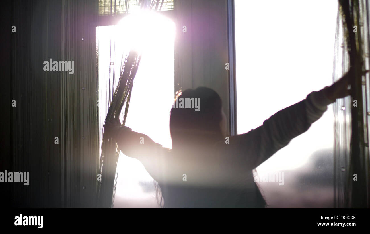 woman opening window curtains on top of the world, back view, sun rays ...