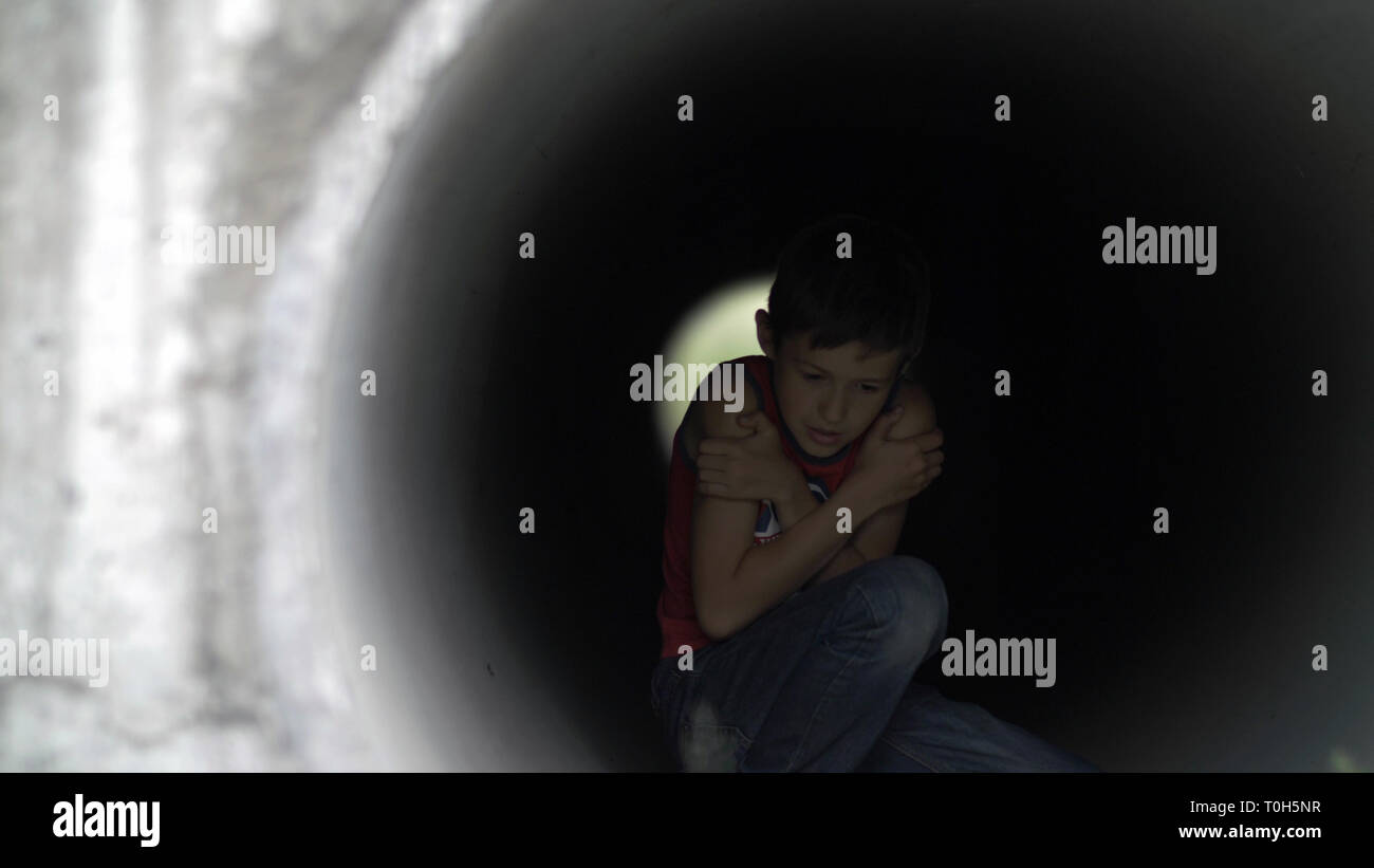 homeless lonely boy hiding inside of a drainage tunnel from the frost ...