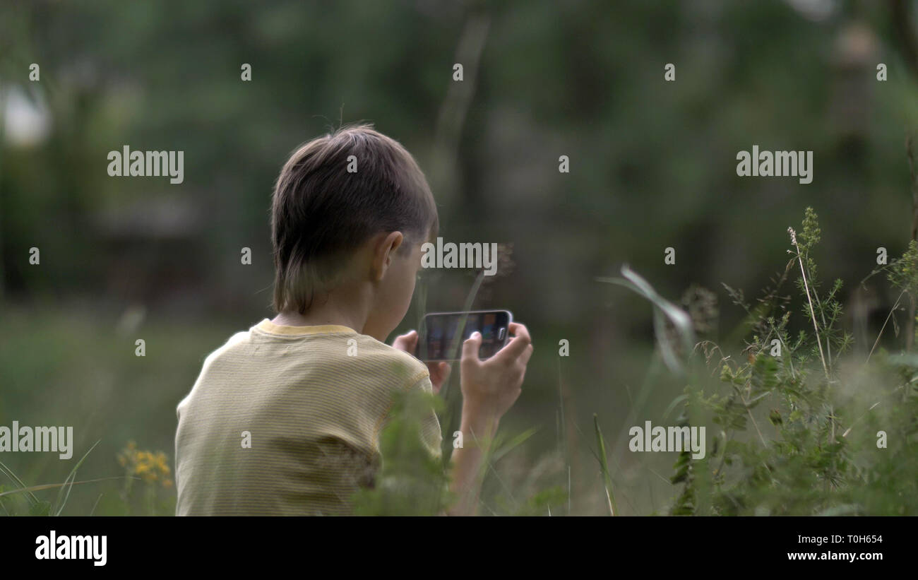 boy hiding and playing in the phone outoors, back view Stock Photo - Alamy
