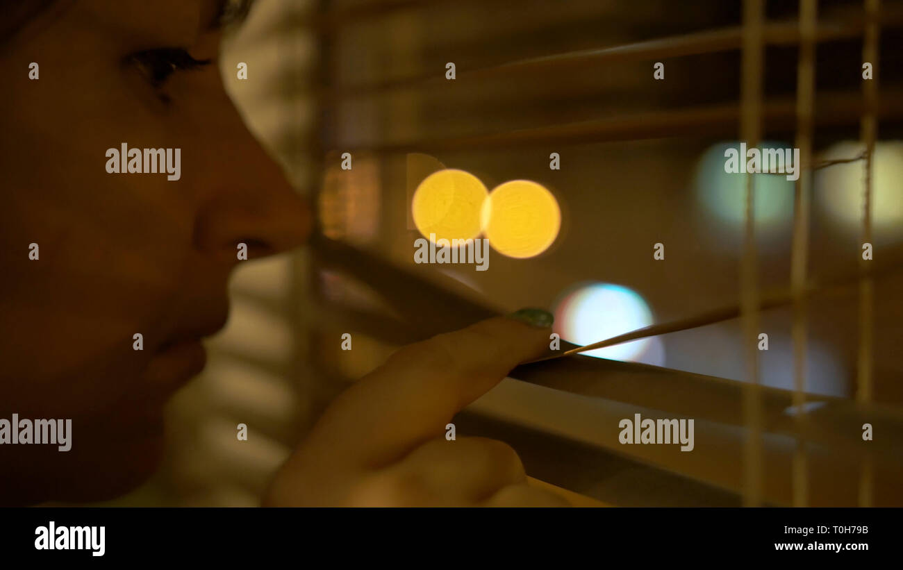 young brunette with brown eyes peeks through the window with her finger ...