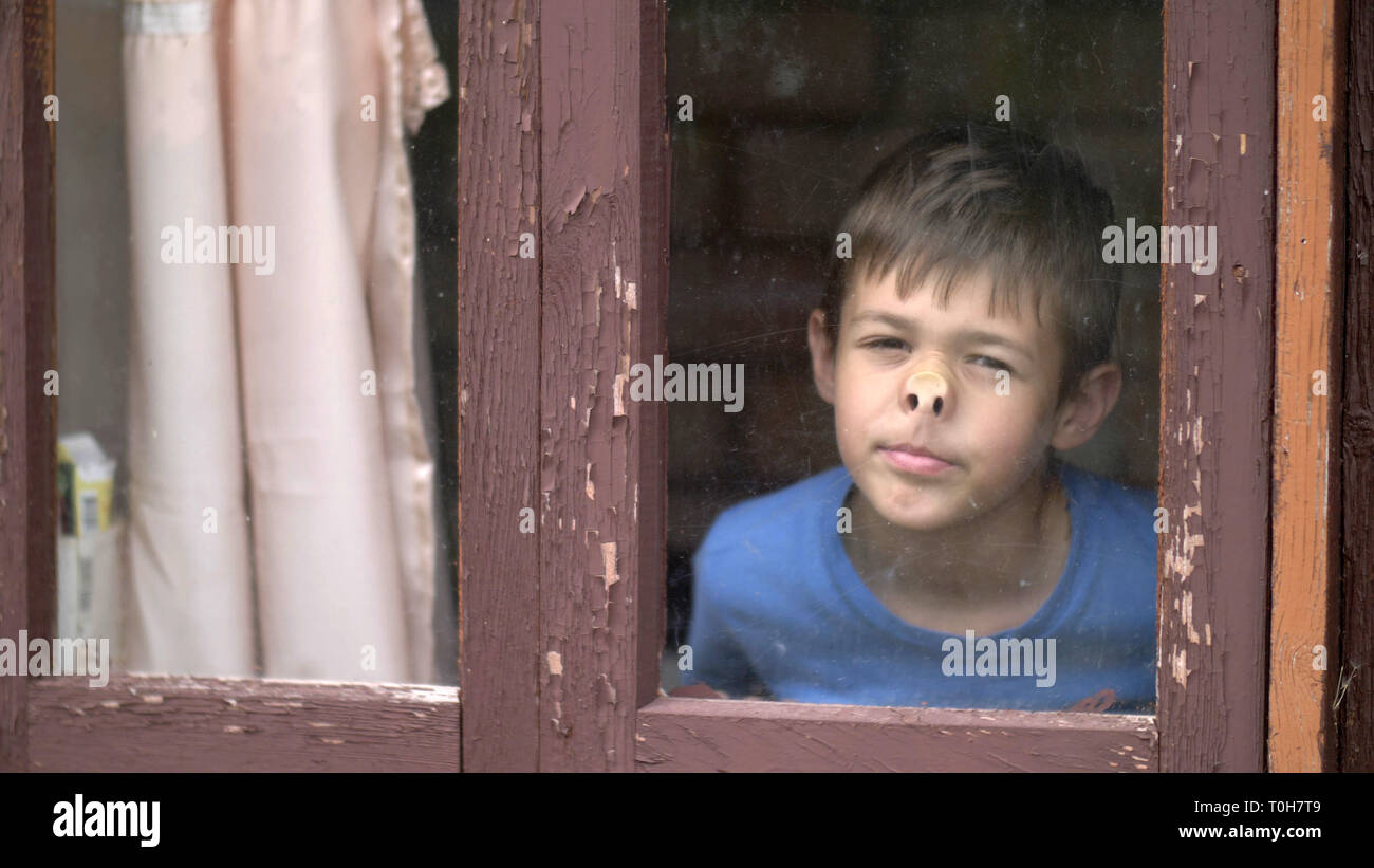funny boy leaned nose to the window at home and looks into the camera ...