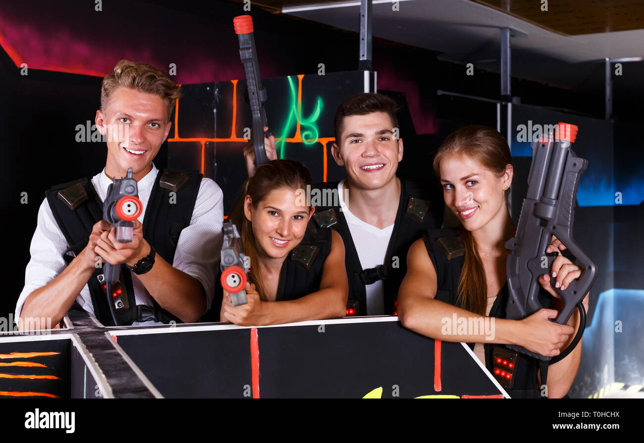 Four happy young male an female posing with laser guns in their hands ...