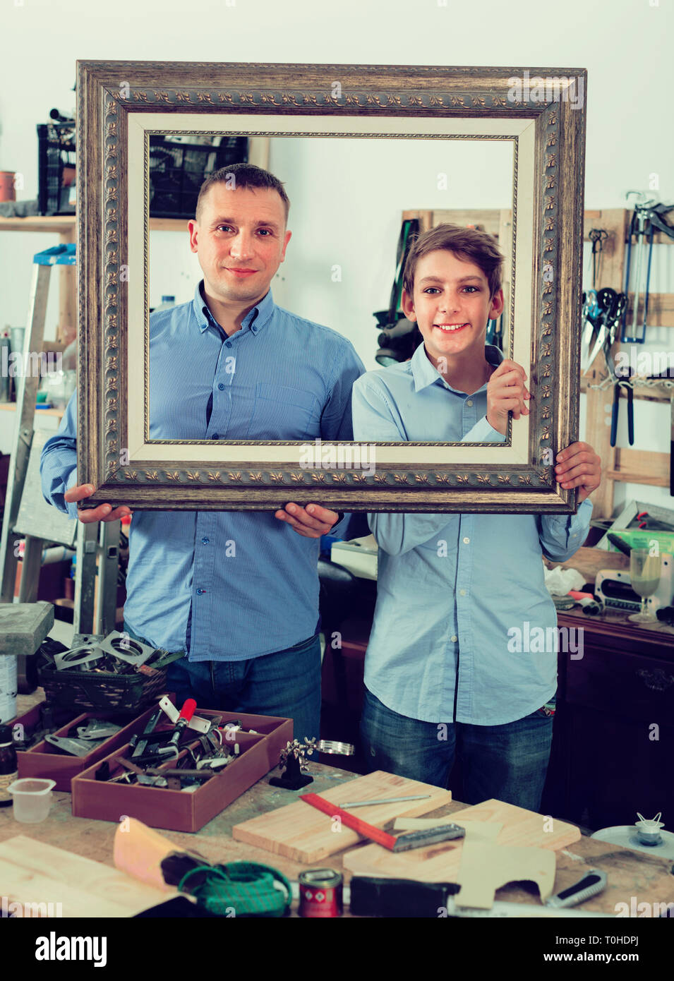 Portrait of happy adult man and boy displaying frame in interior studio ...