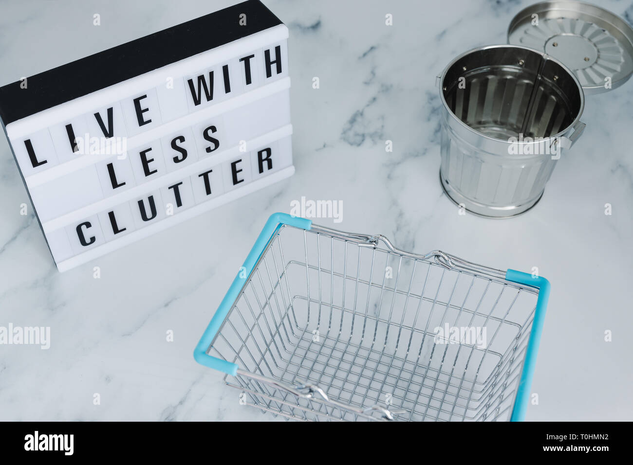 ecology and consumerism concept: live with less clutter message on lightbox with shopping basket ...