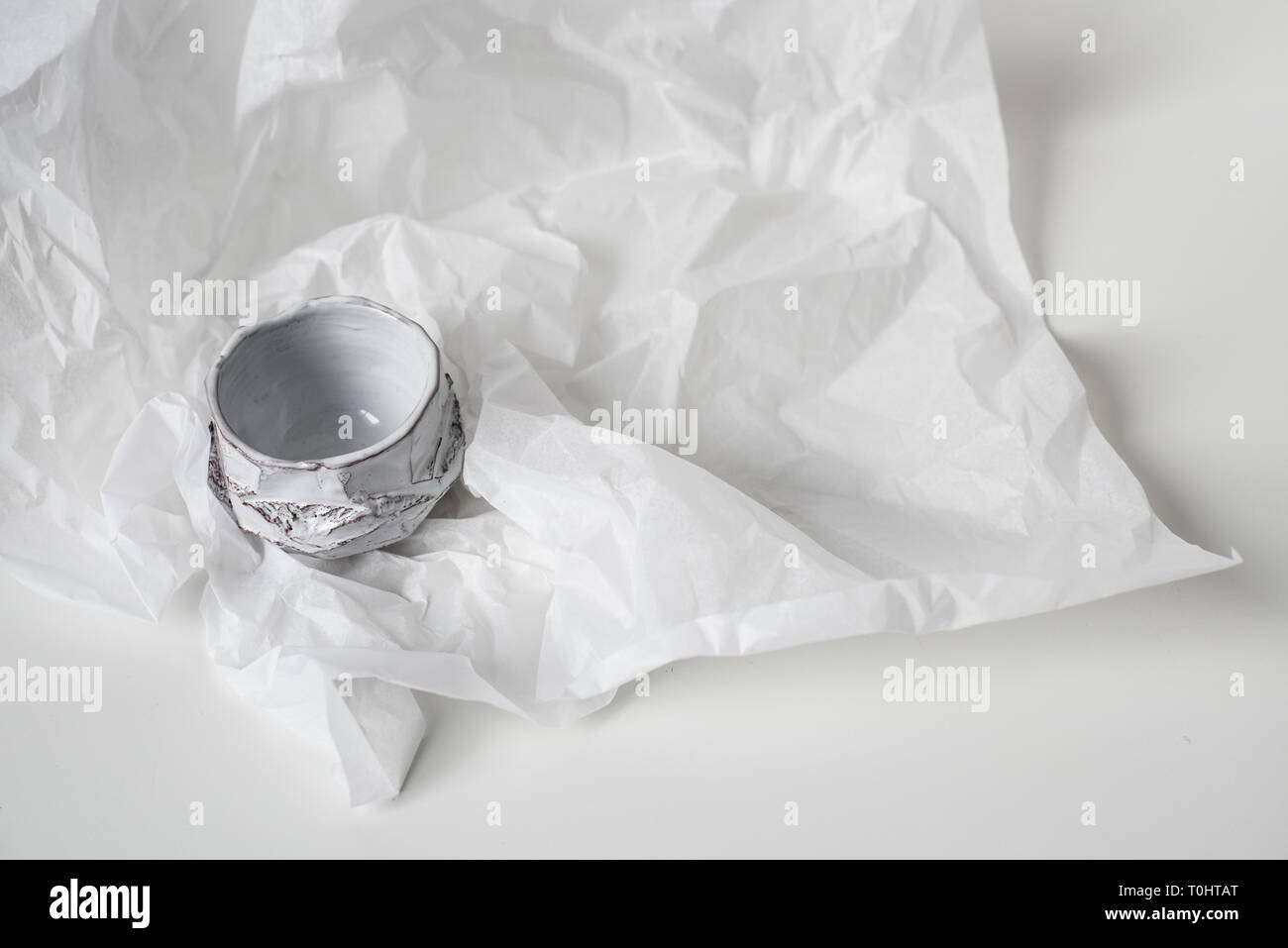 Handmade ceramic vase on dented white paper close-up daylight studio ...
