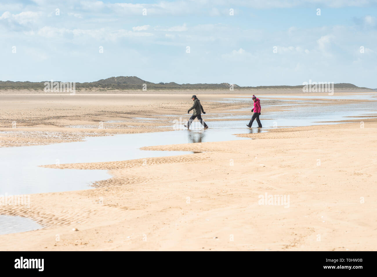 Hikers cross water pools left by the tide on sandy beach at Holkham bay ...