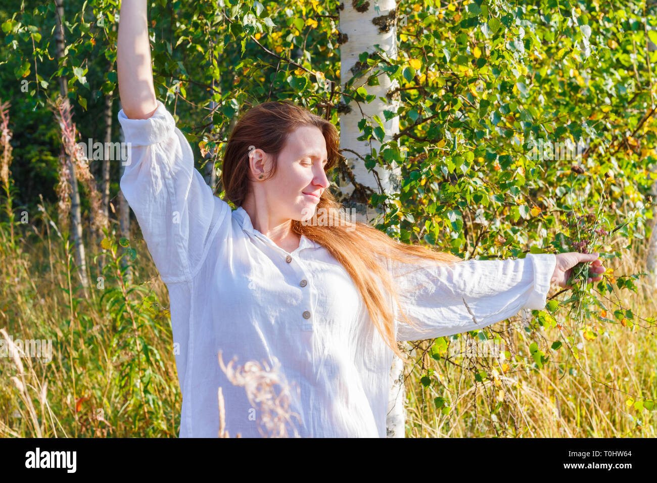 The smiling girl in a white shirt with the placed hands in summer wood ...