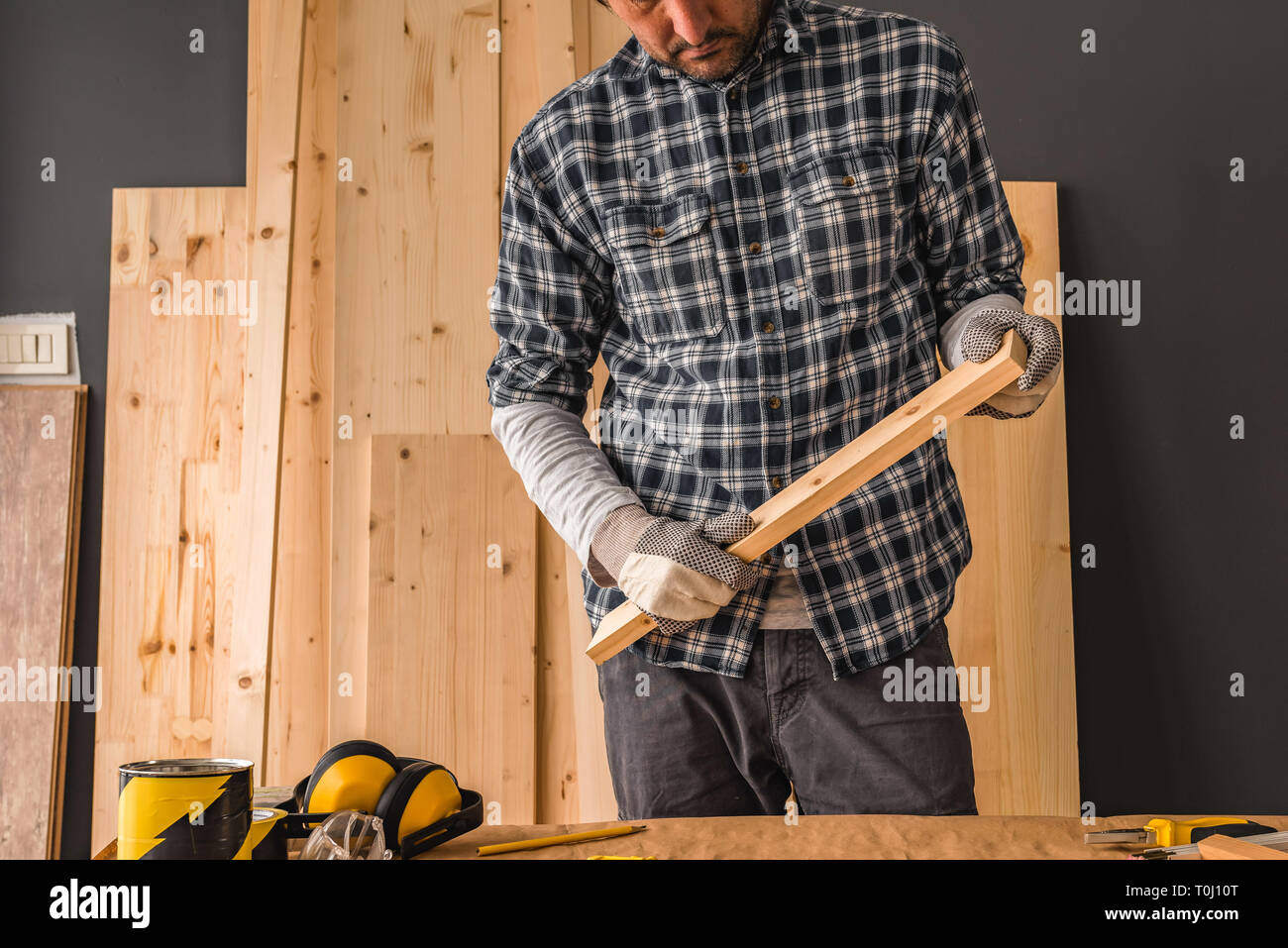 Carpenter is holding small pine plank in workshop over his working desk ...