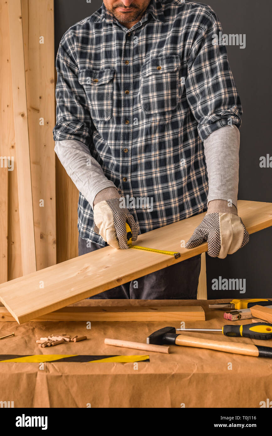 Carpenter is measuring pine wood plank with tape measure for woodwork ...