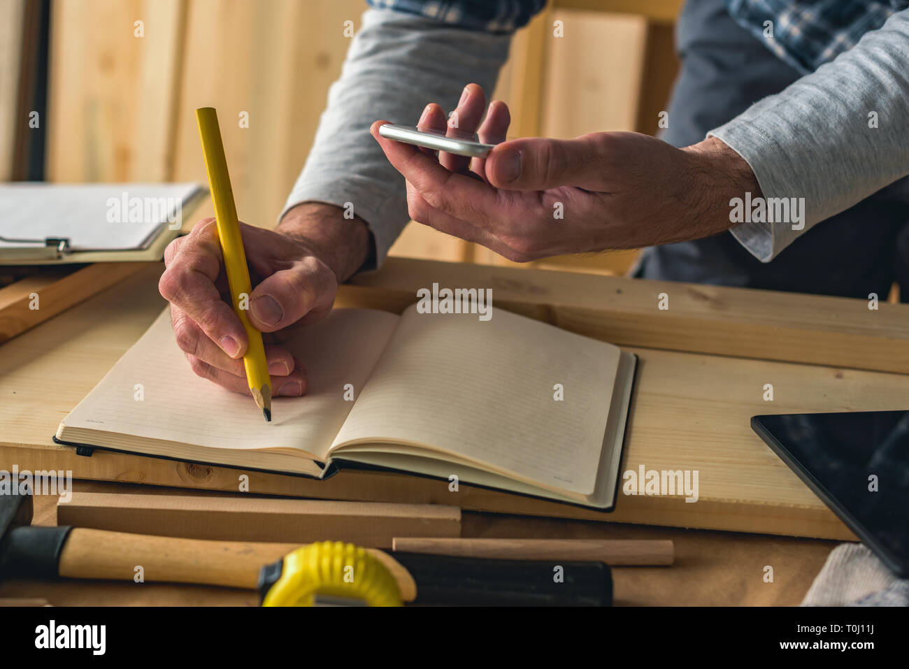 Carpenter is writing project notes while using smartphone in small ...