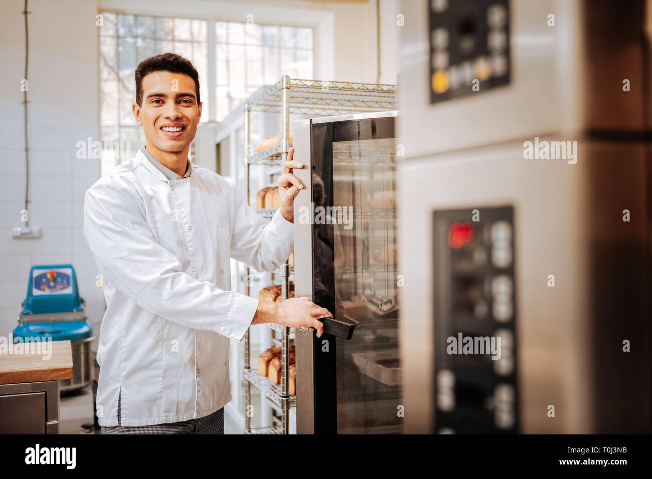 Baker smiling while opening the door on oven and checking bread Stock ...