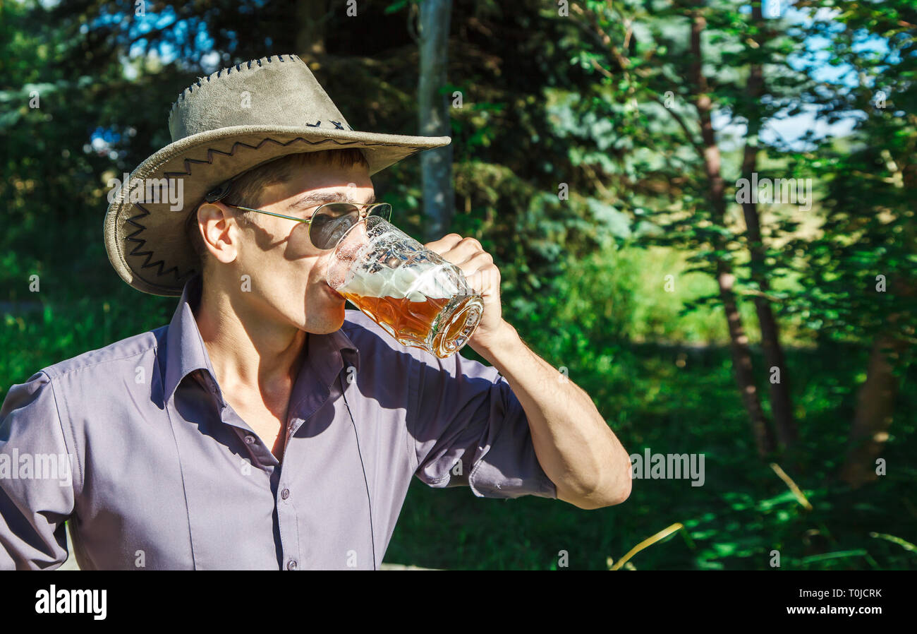 young man in a cowboy hat and sunglasses is drinking beer in the park ...