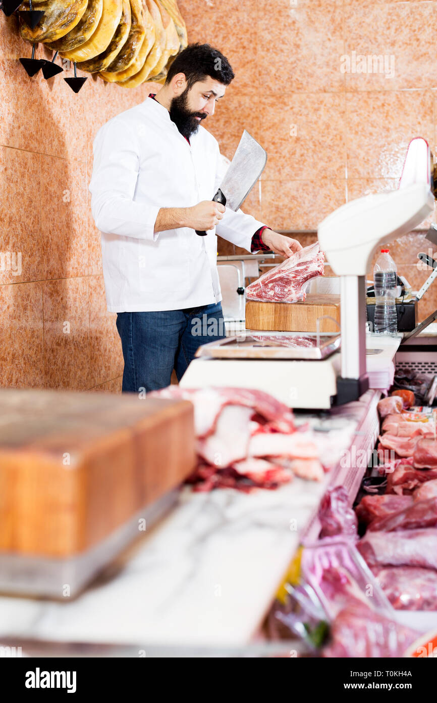 Happy young male seller cutting meat to sell in butcher’s shop Stock ...