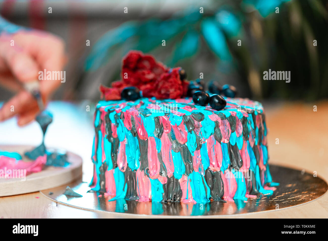 Close up of tattooed man decorating cake with butter colourful cream ...