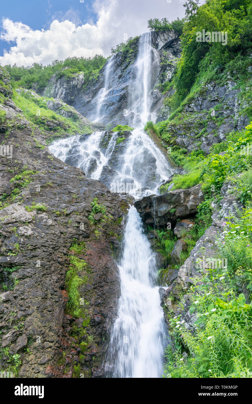 High waterfall with a powerful stream falling from a green cliff ...