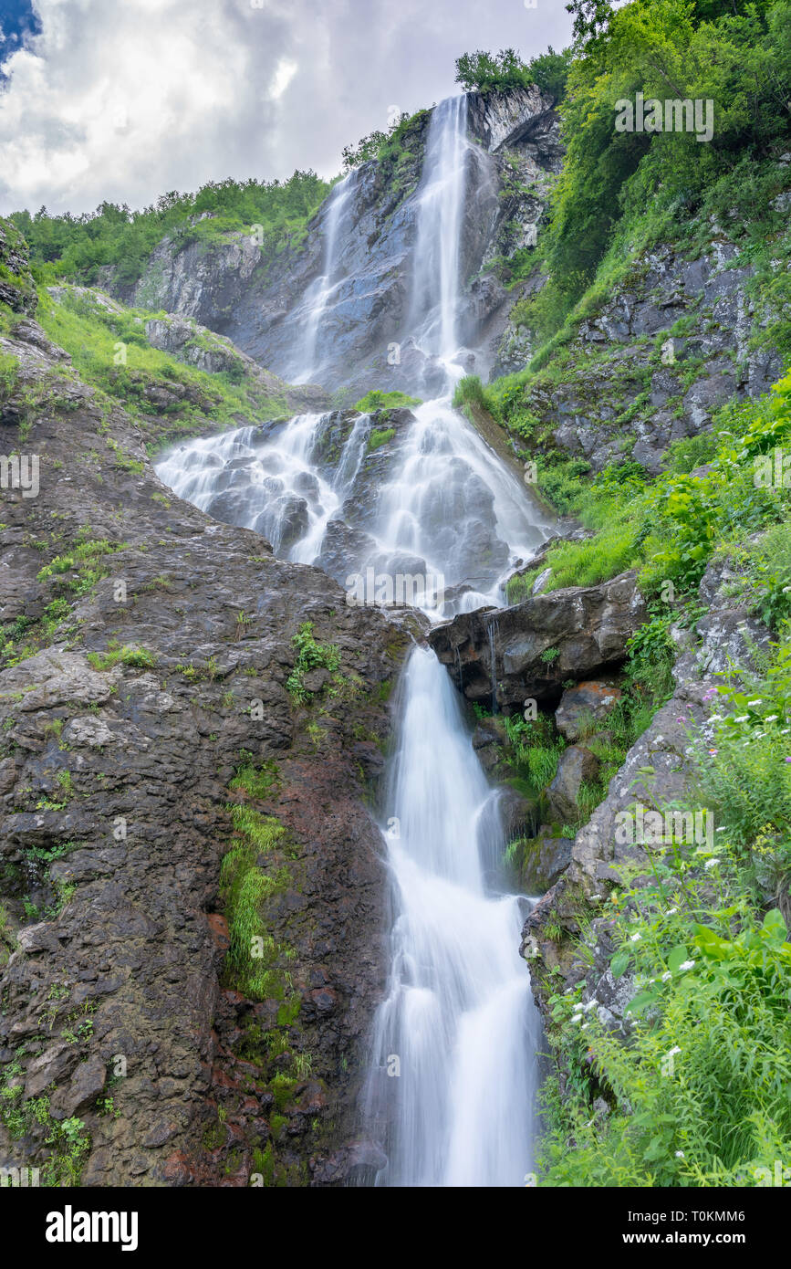 High waterfall with a powerful stream falling from a green cliff ...