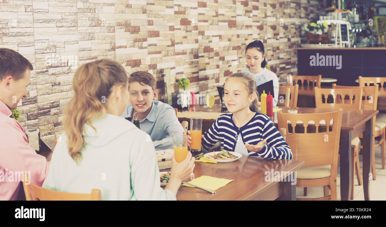 Glad parents with children having conversation at dining table in cafe ...