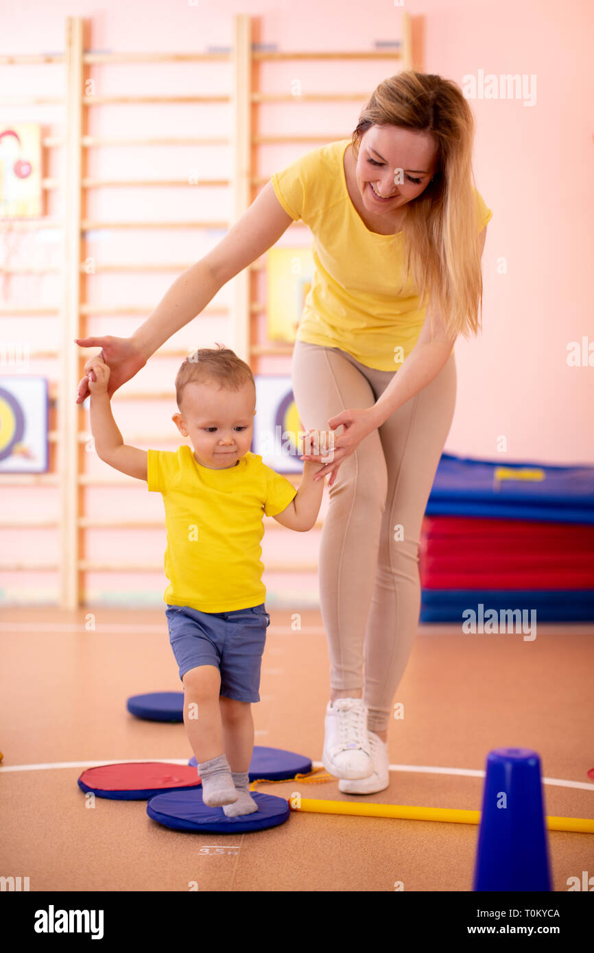 little kid doing steps on fitness plate with trainer's help in the gym ...
