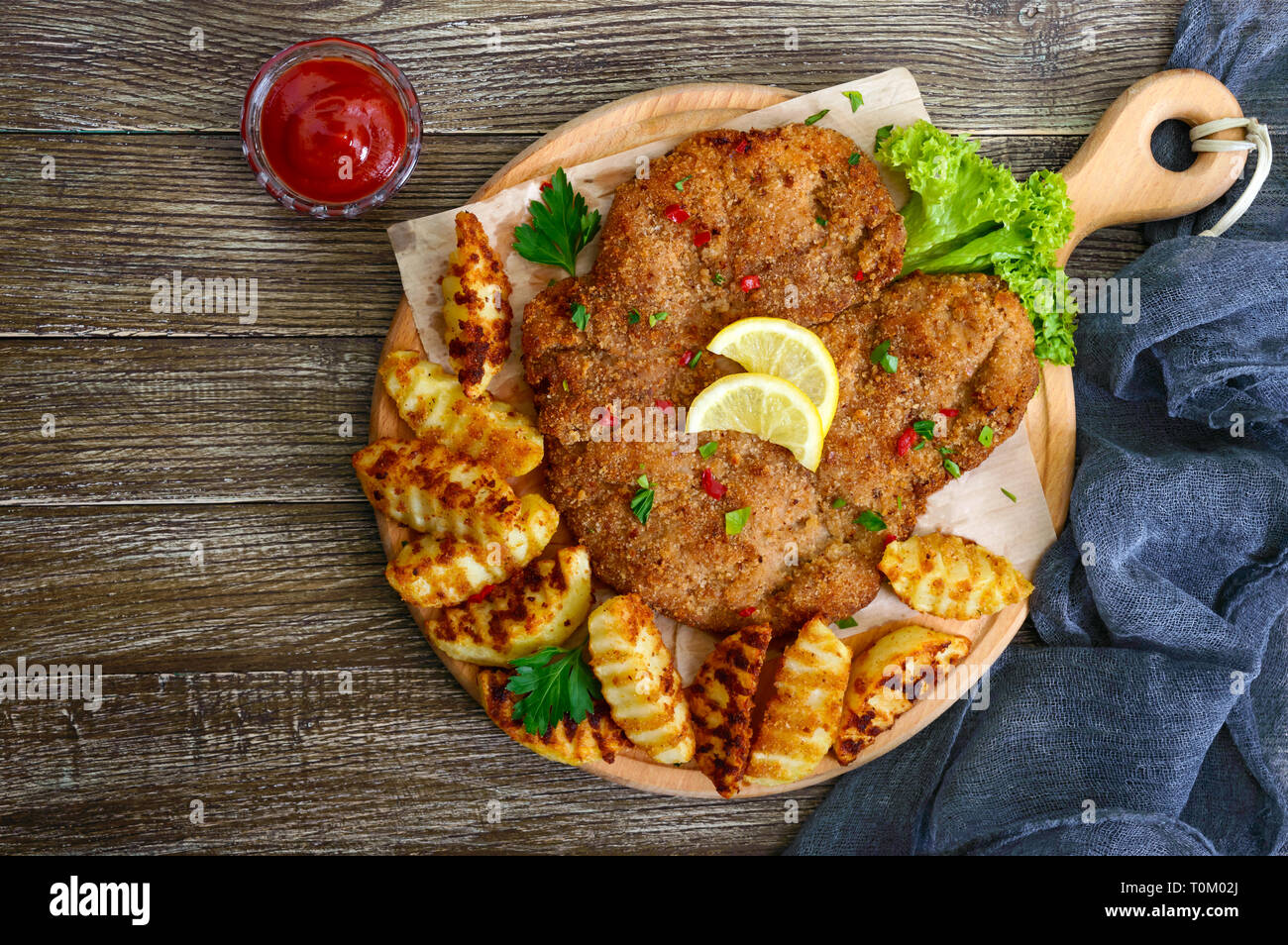 Large schnitzel with baked golden potatoes on a wooden cutting board ...