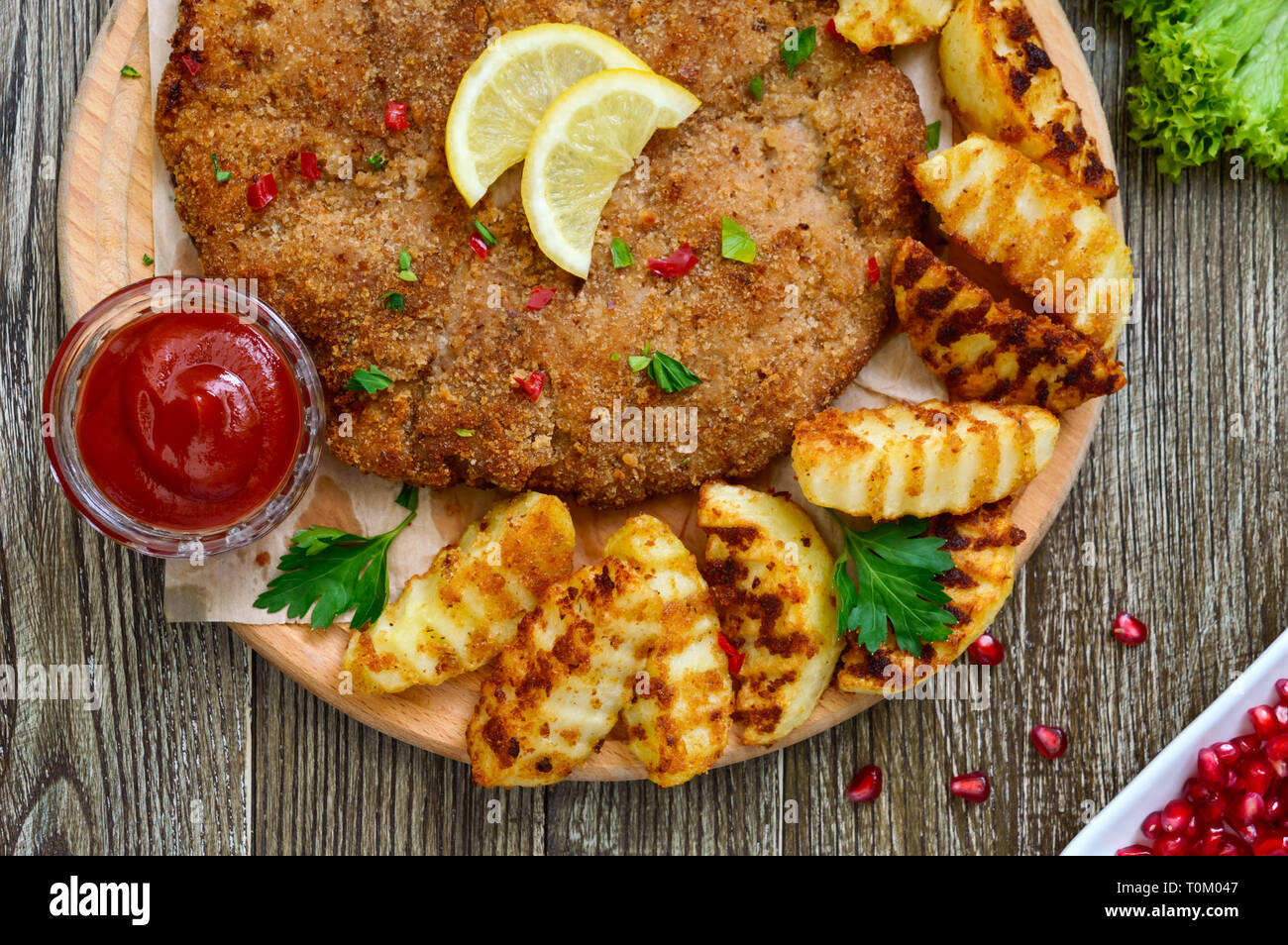Large schnitzel with baked golden potatoes on a wooden cutting board ...