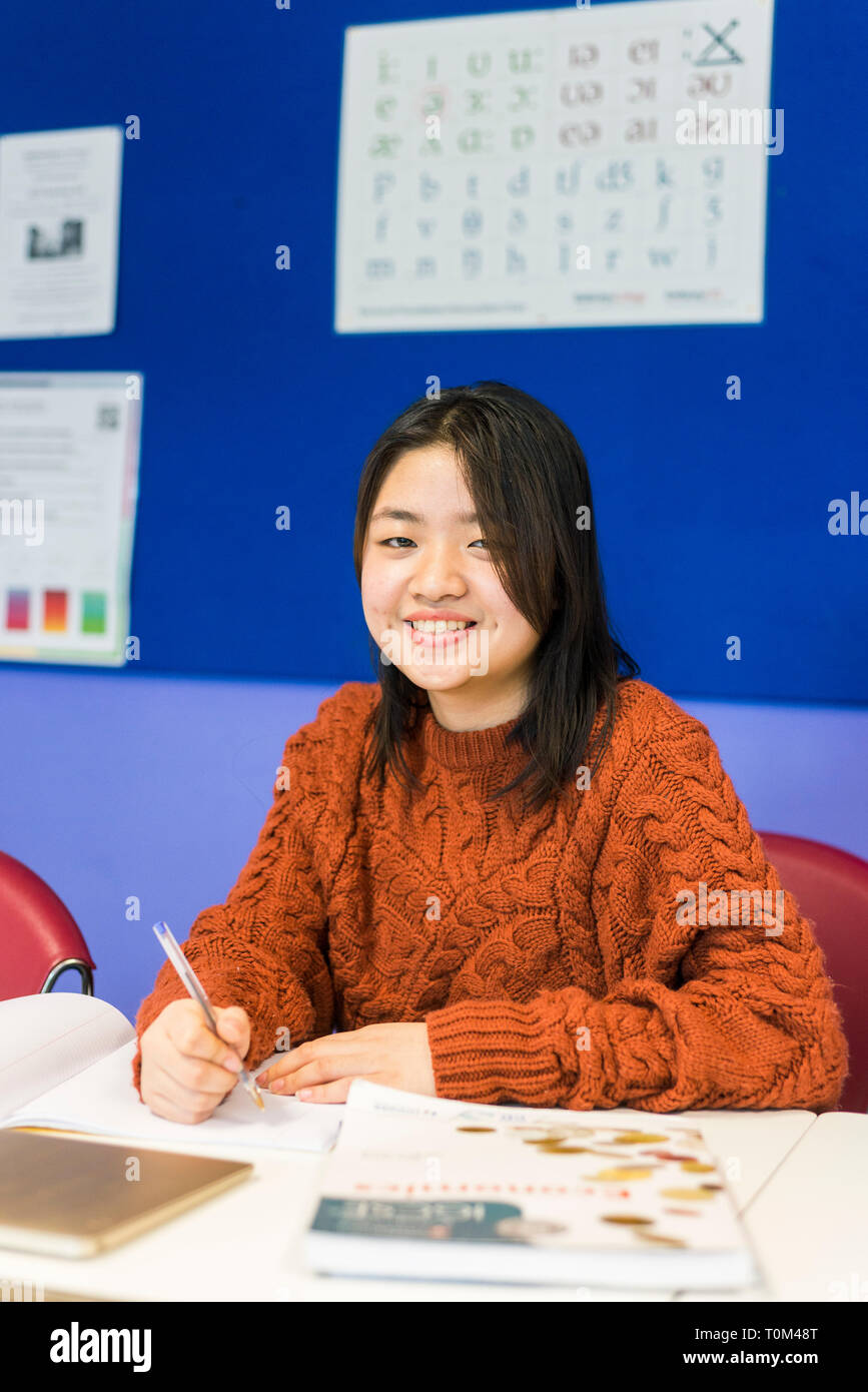 A young international Asian student sits at a desk in a classroom ...