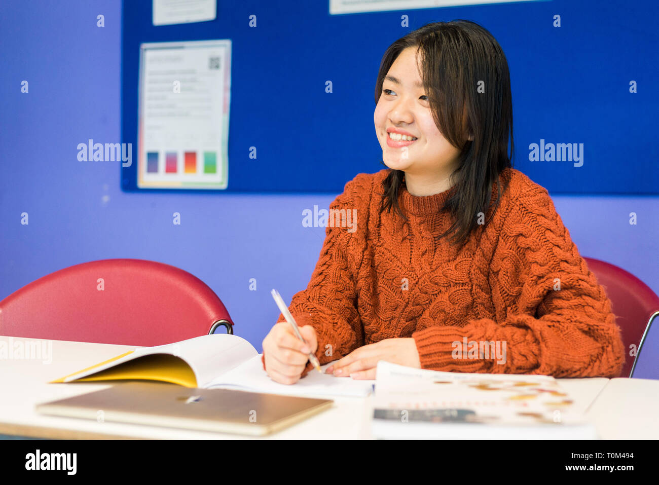 A young international Asian student sits at a desk in a classroom ...