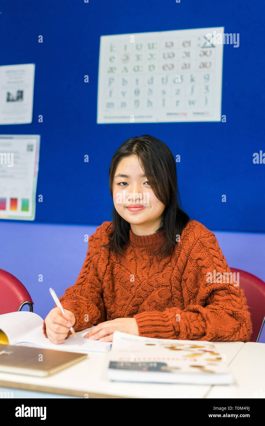A young international Asian student sits at a desk in a classroom ...