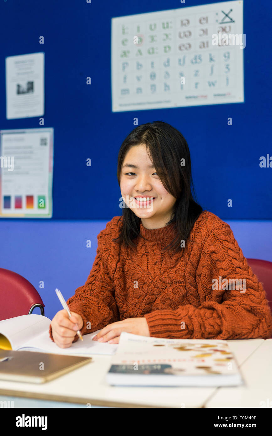 A young international Asian student sits at a desk in a classroom ...