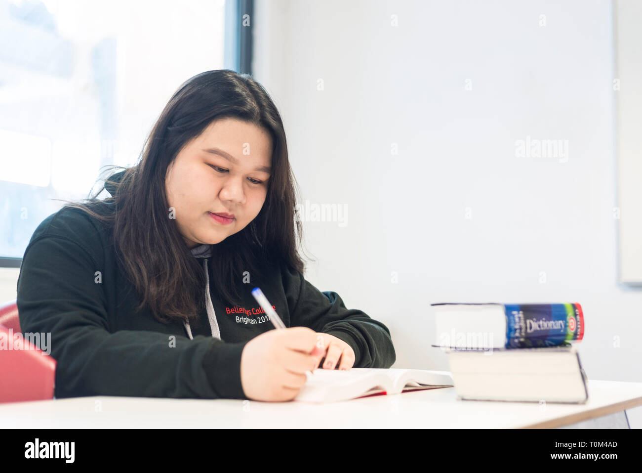A young international Asian student sits at a desk in a classroom ...