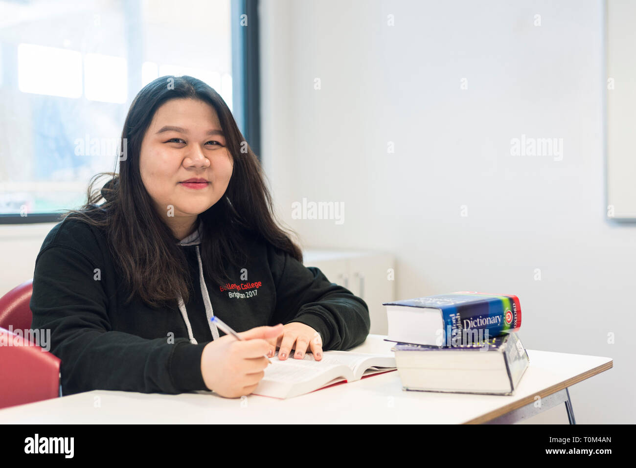 A young international Asian student sits at a desk in a classroom ...