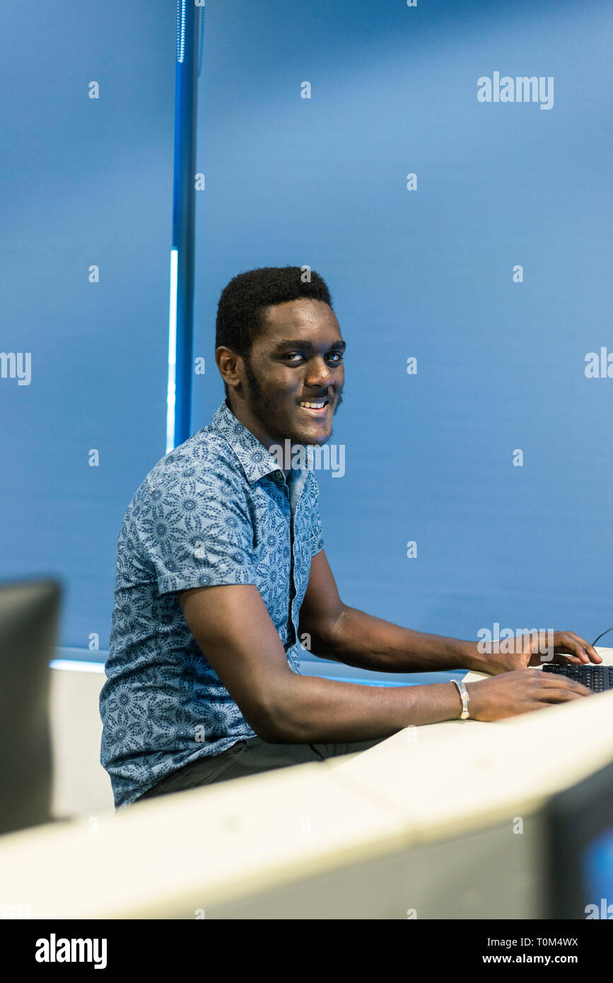 A young black man sits at a desk in the computer room of a college ...
