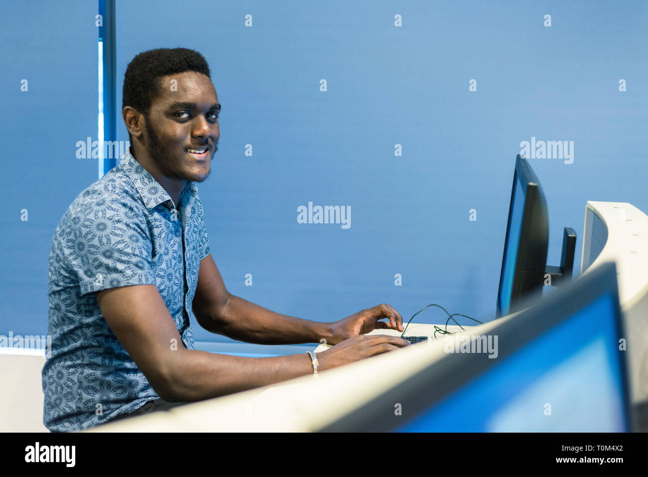 A young black man sits at a desk in the computer room of a college ...