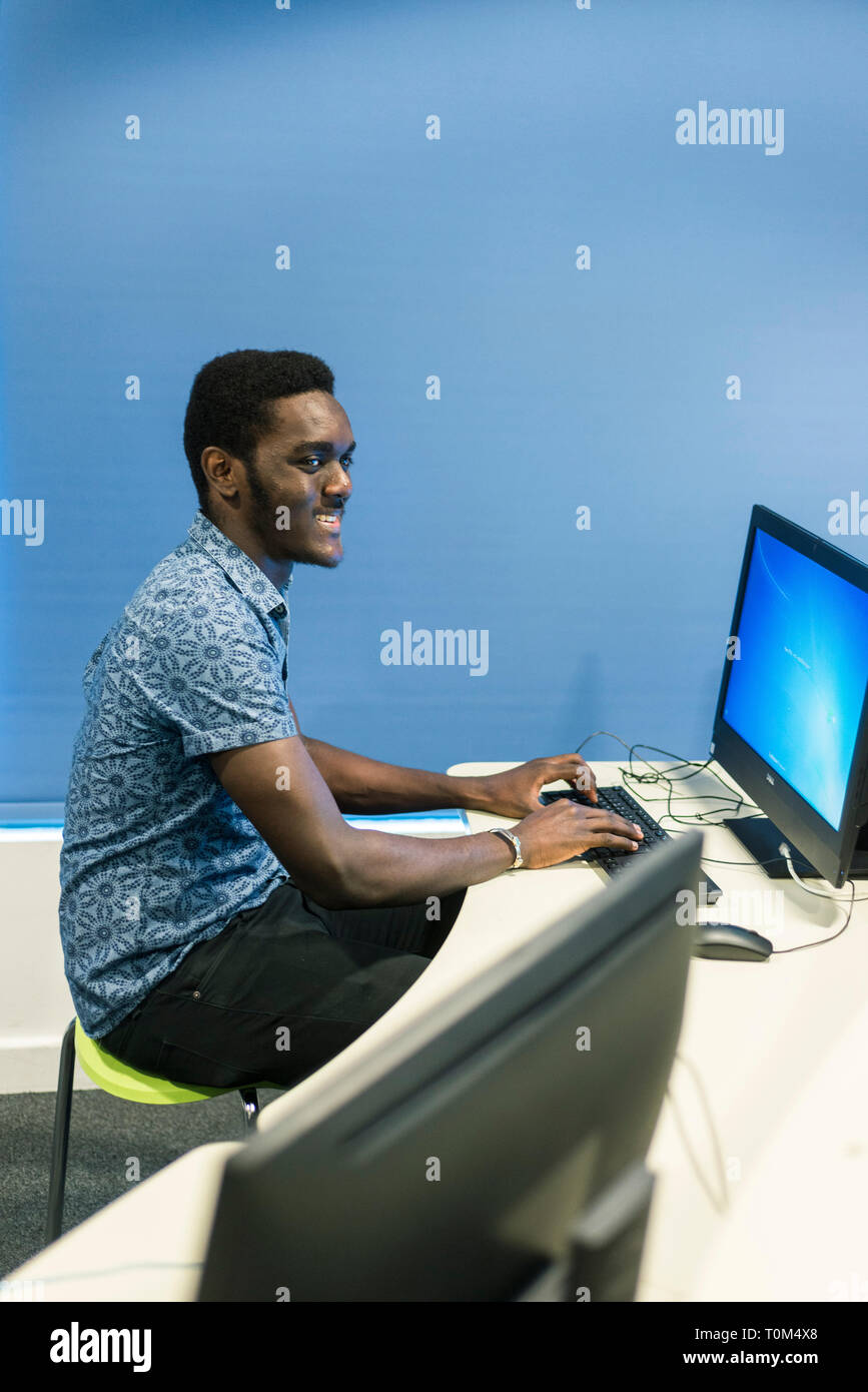 A young black man sits at a desk in the computer room of a college ...