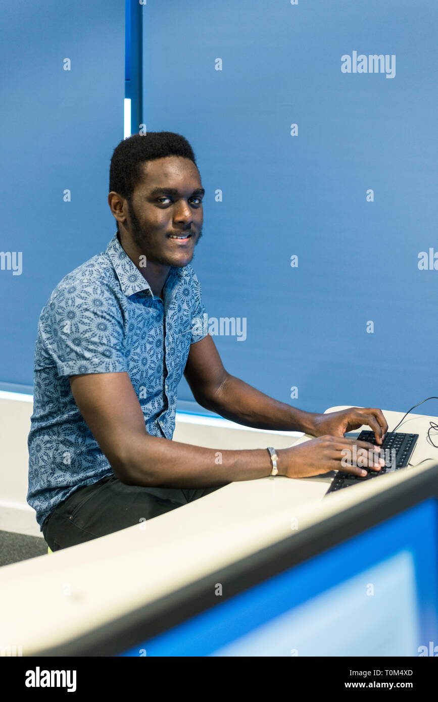 A young black man sits at a desk in the computer room of a college ...