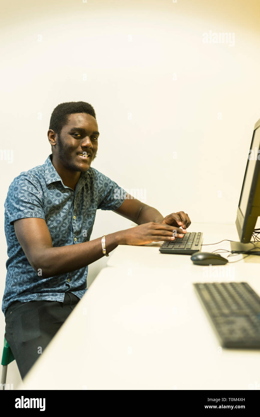 A young black man sits at a desk in the computer room of a college ...
