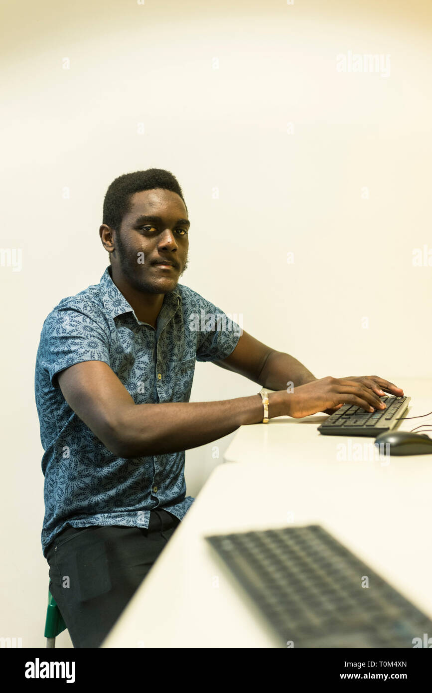 A young black man sits at a desk in the computer room of a college ...