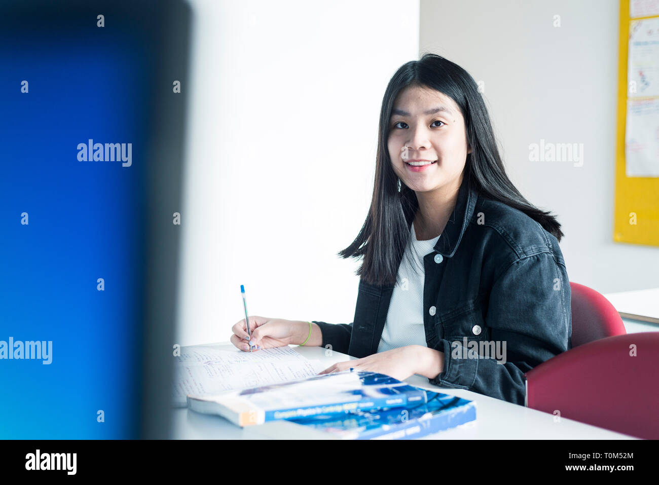 A young international Asian student sits at a desk in a classroom ...
