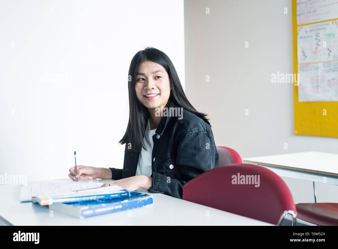 A young international Asian student sits at a desk in a classroom ...