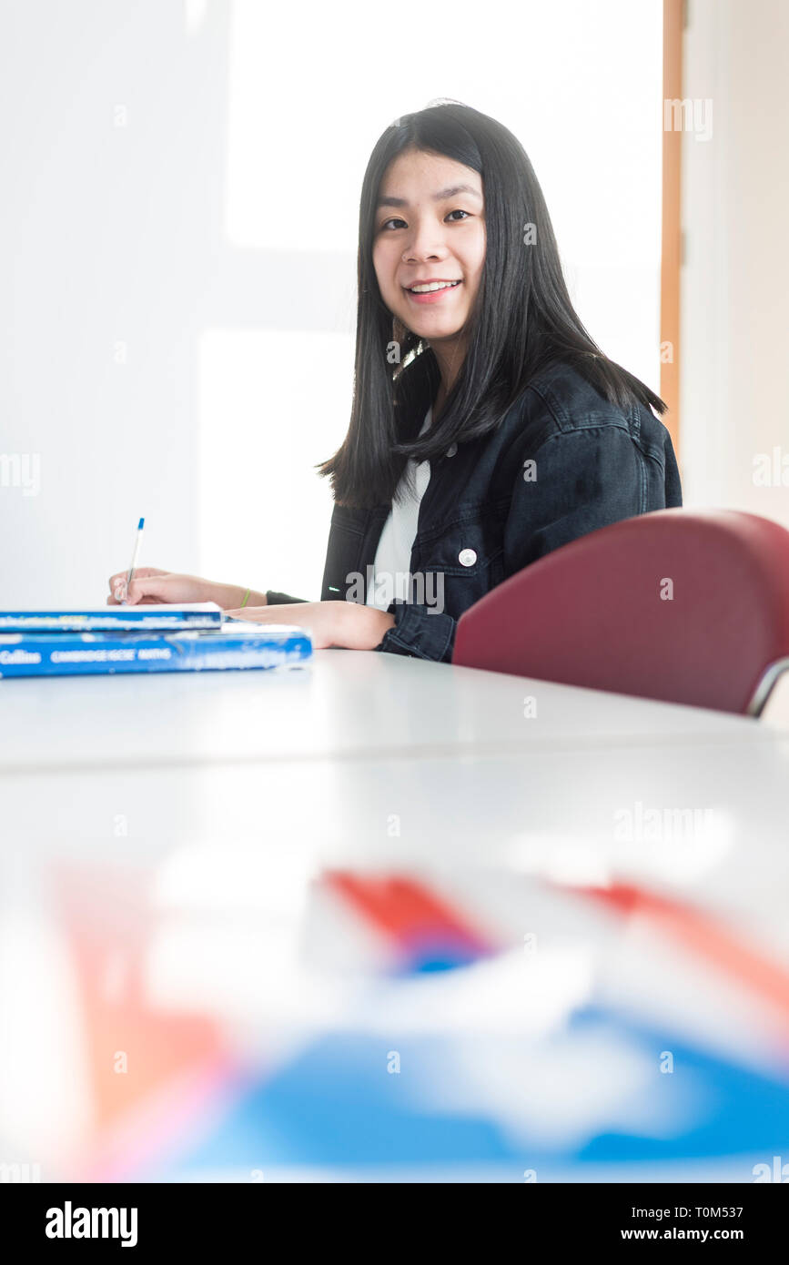 A young international Asian student sits at a desk in a classroom ...