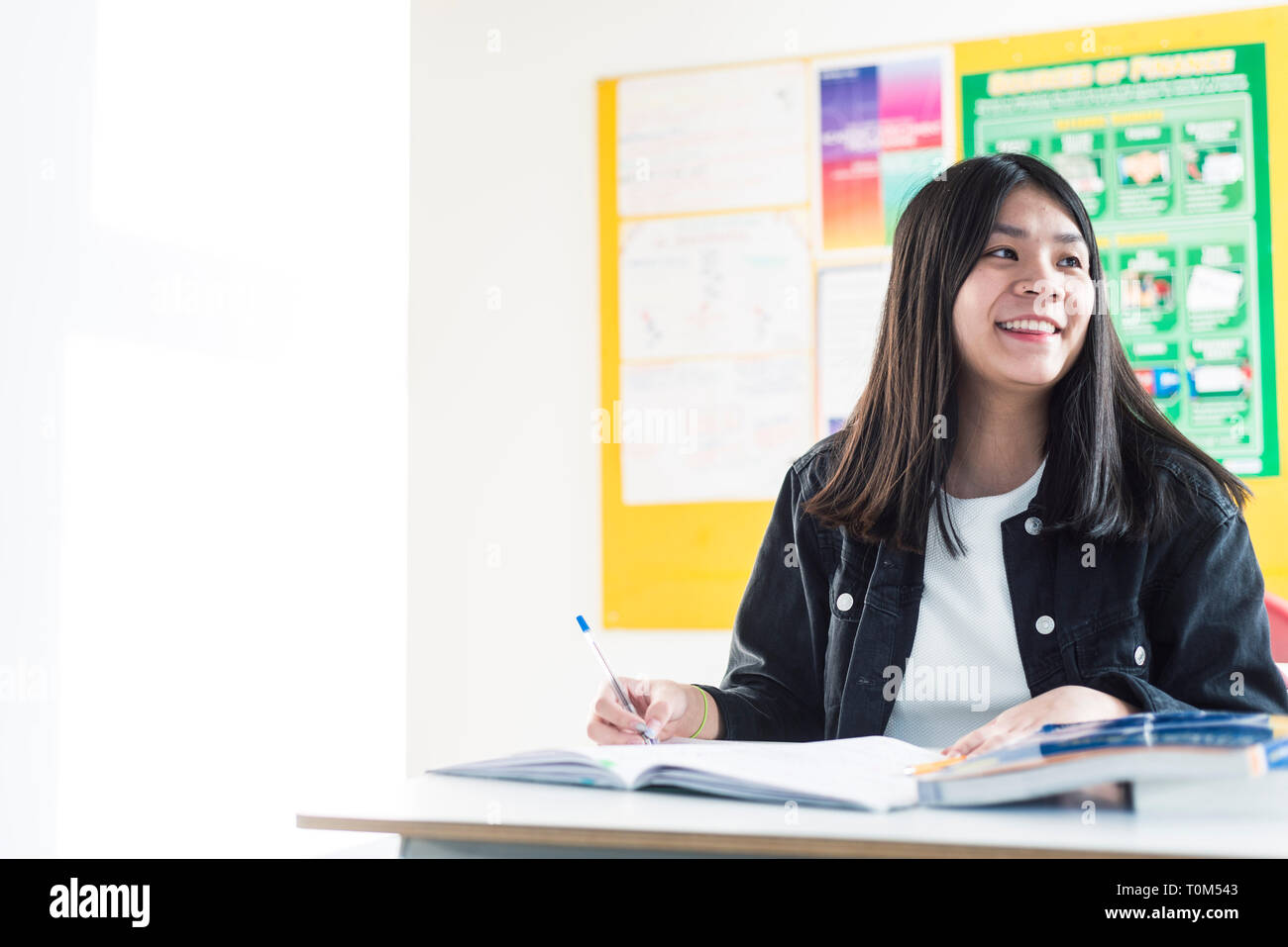 A young international Asian student sits at a desk in a classroom ...
