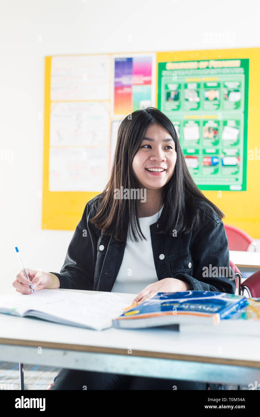 A young international Asian student sits at a desk in a classroom ...