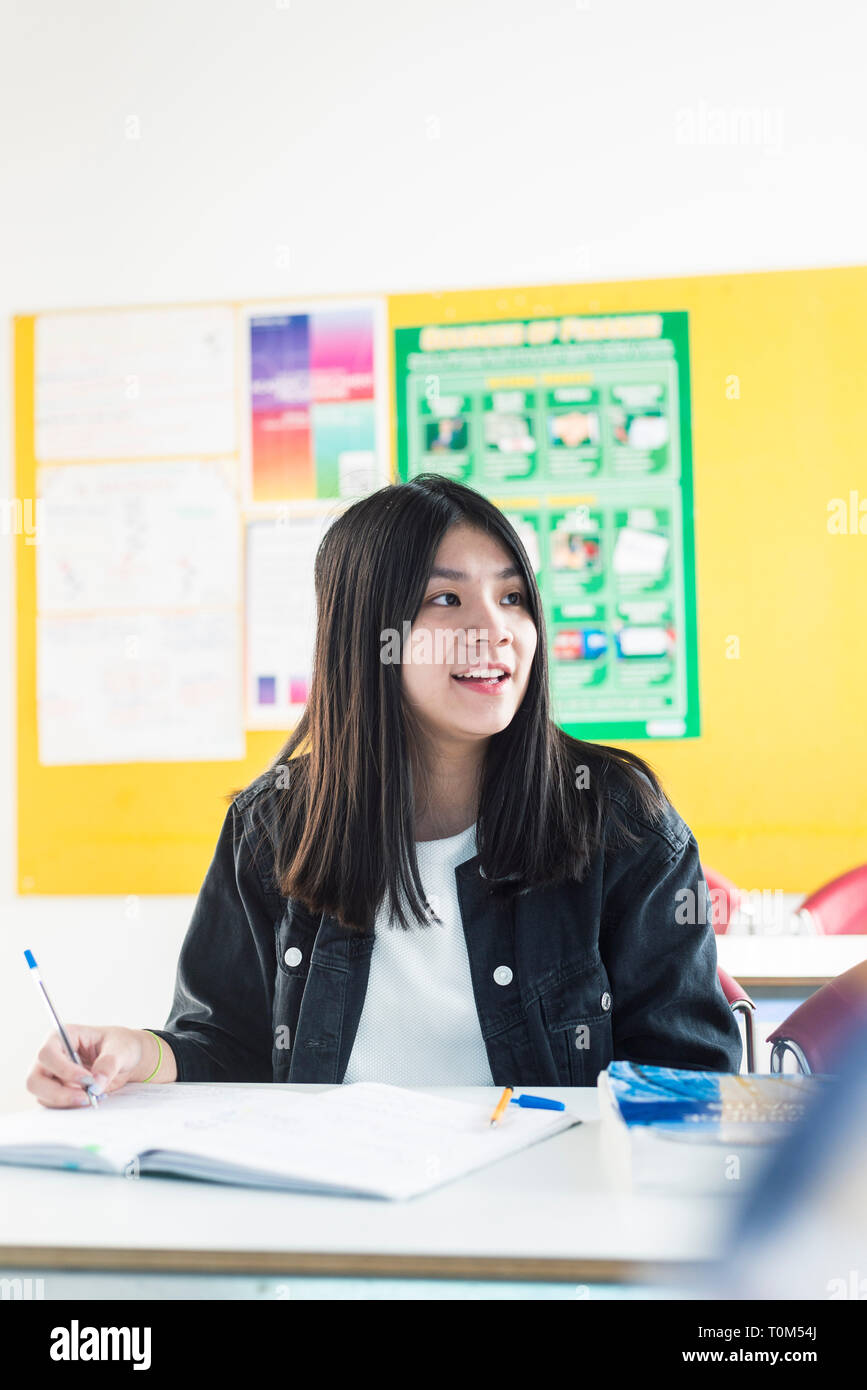A young international Asian student sits at a desk in a classroom ...