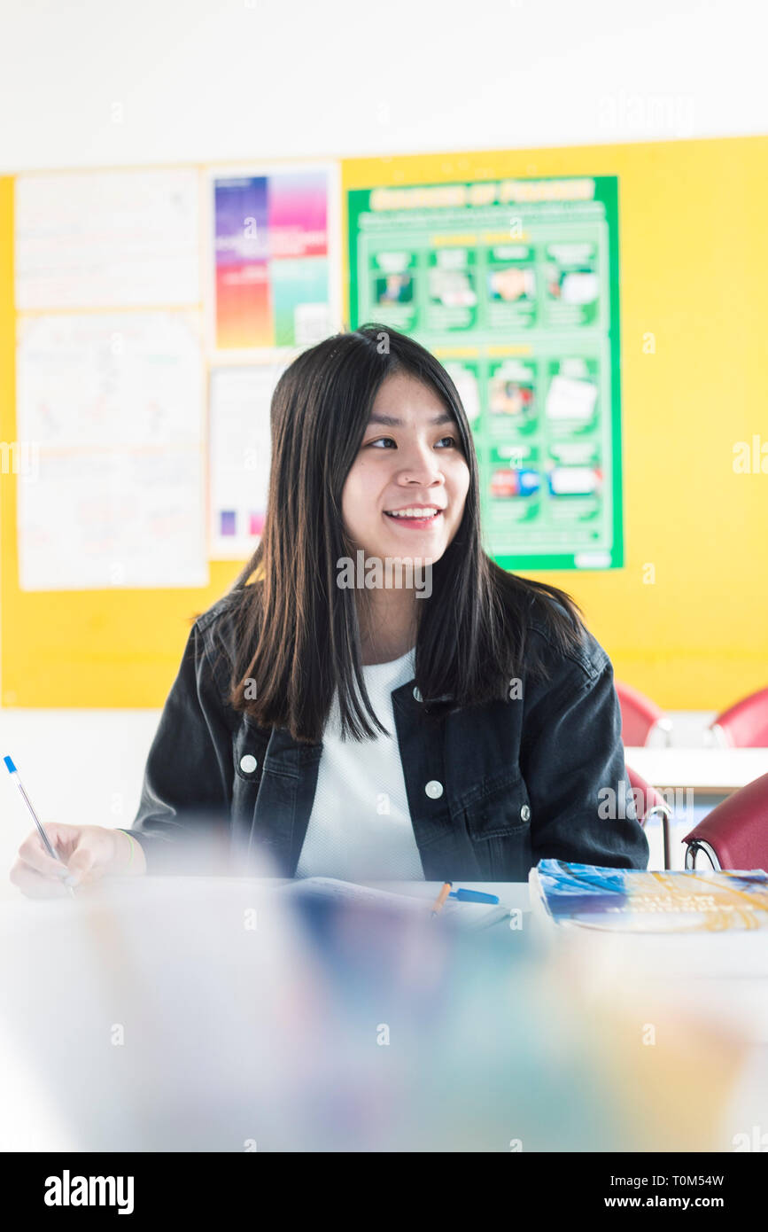 A young international Asian student sits at a desk in a classroom ...