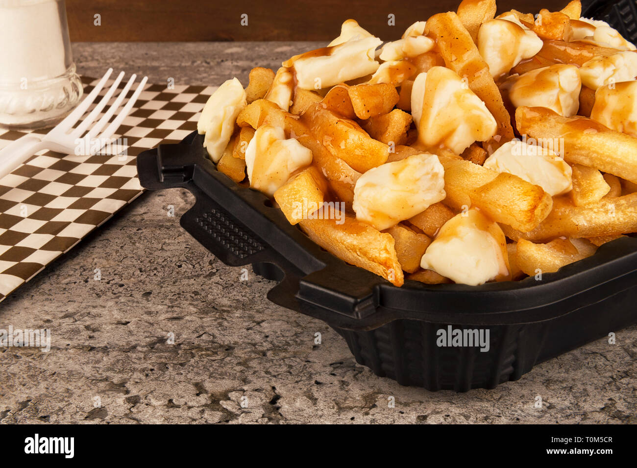 Poutine in a takeout container. Cooked with french fries, beef gravy ...